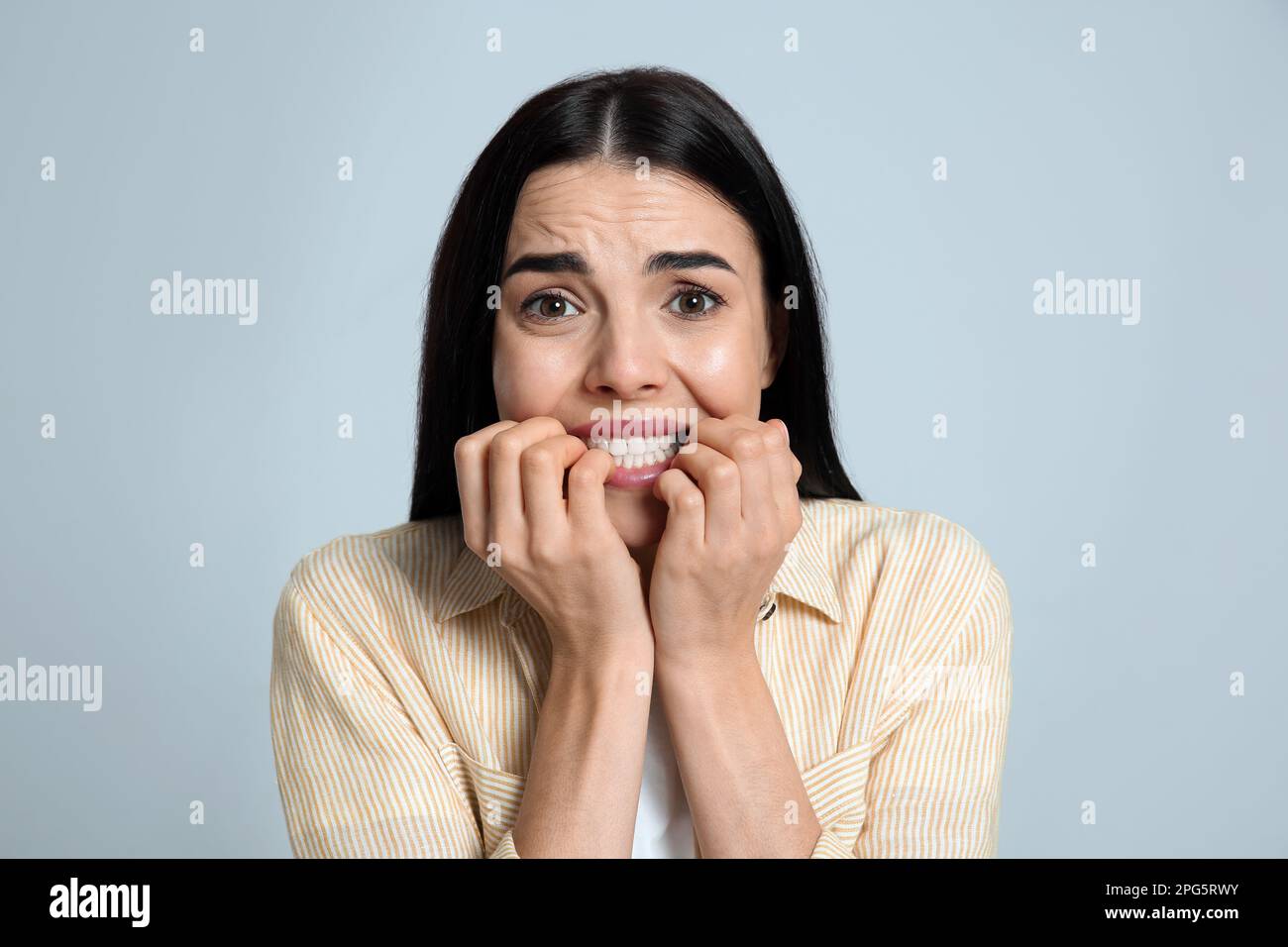 Scared young woman biting her nails on light grey background Stock ...