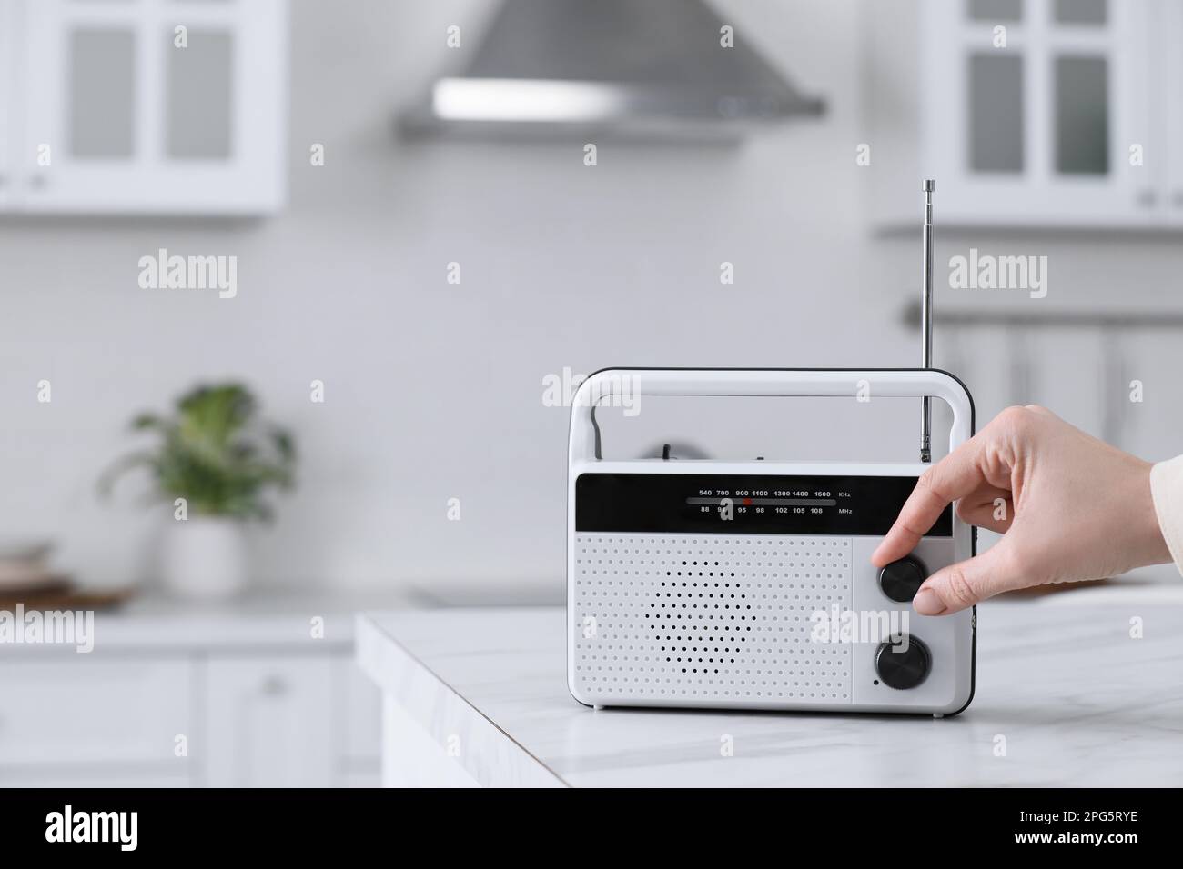 Woman turning volume knob on radio in kitchen, closeup. Space for text ...