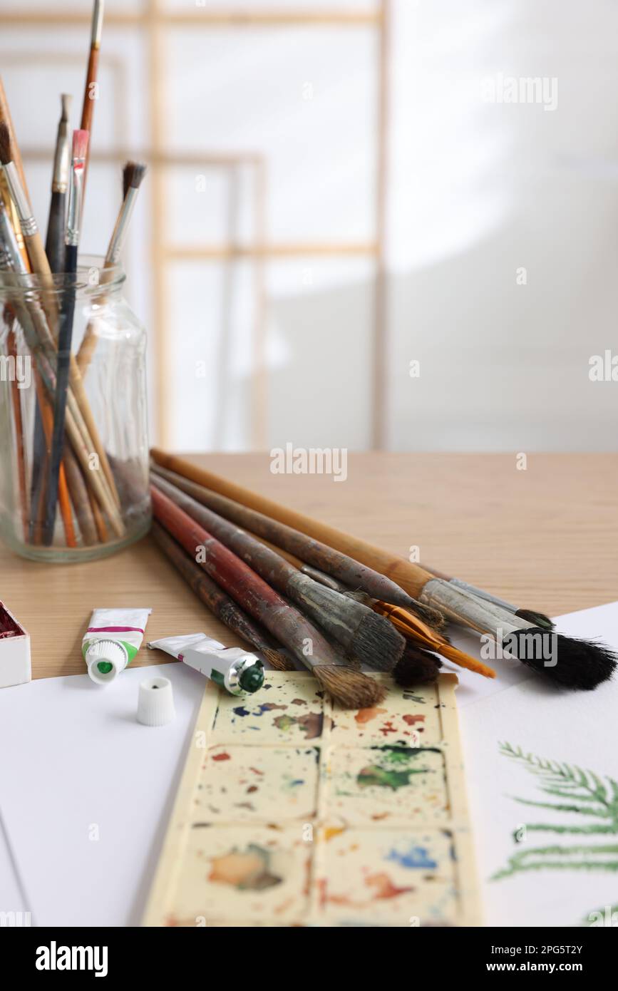 Different brushes, colorful paints, palette and drawing on table in ...
