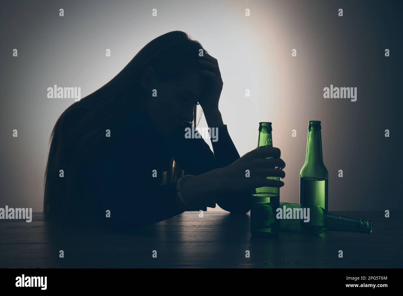 Alcohol addiction. Silhouette of woman holding beer bottle at table ...