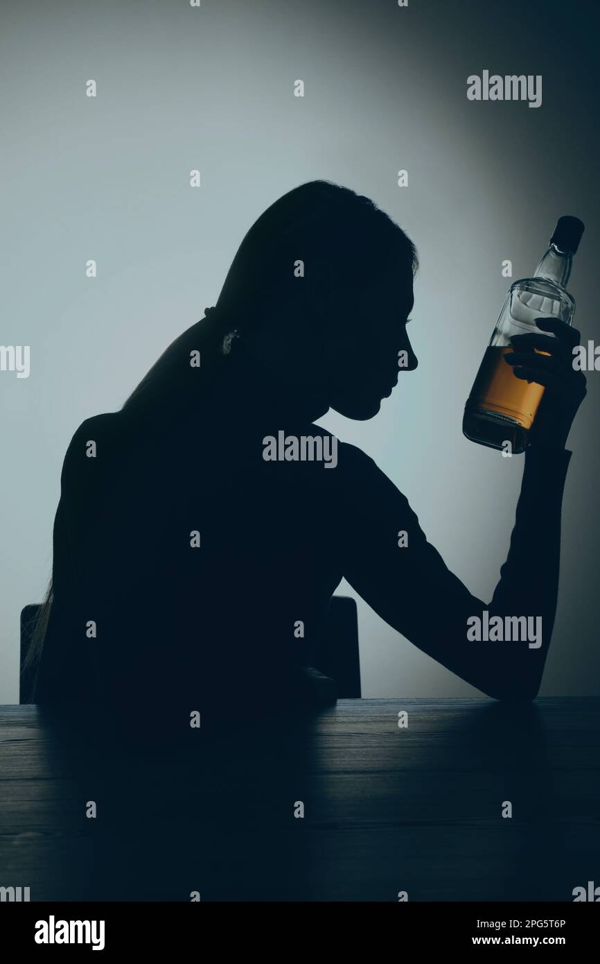 Alcohol addiction. Silhouette of woman with bottle of whiskey at wooden ...
