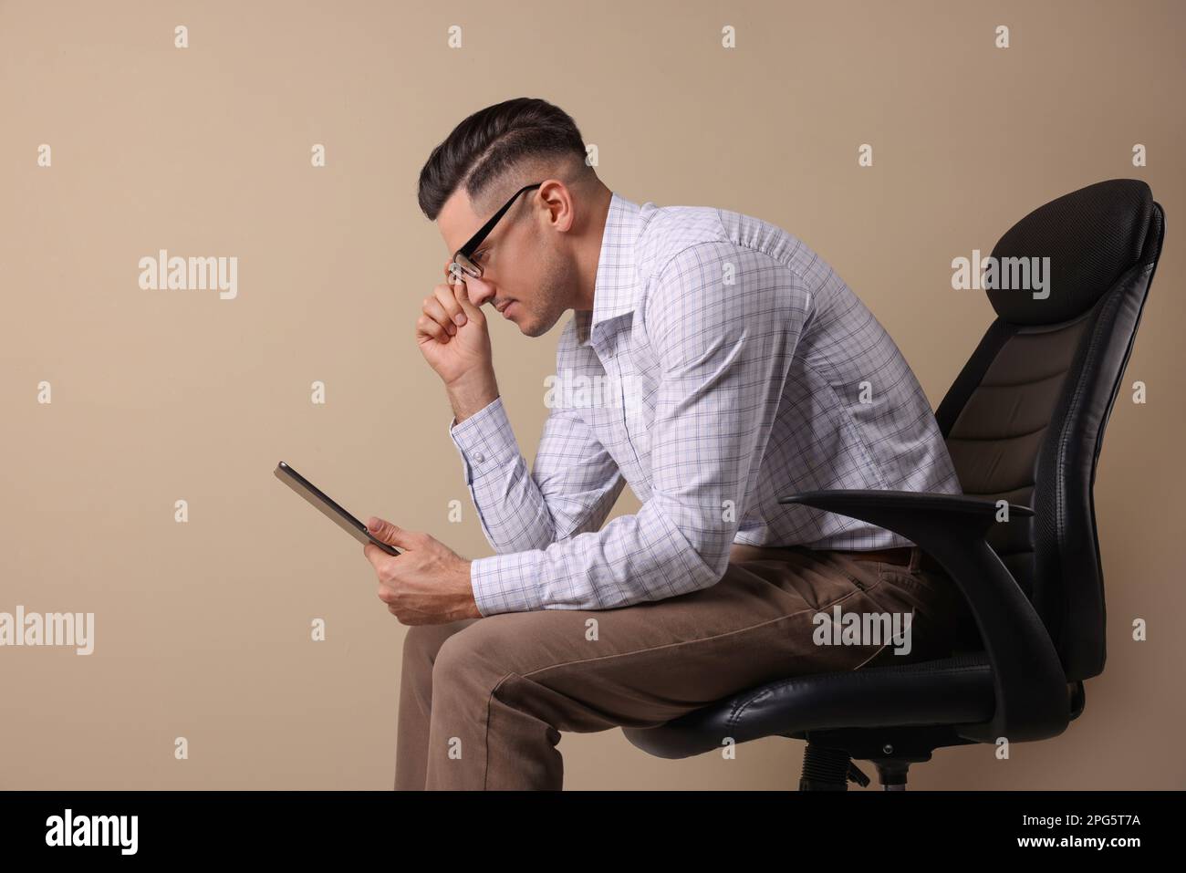 Man with poor posture using tablet while sitting on chair against beige ...