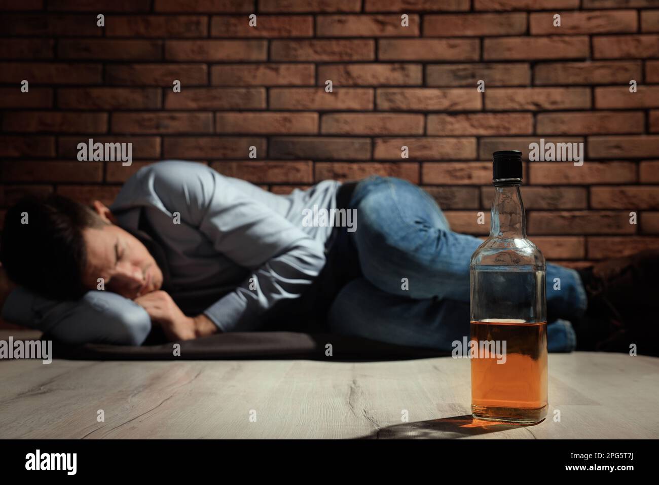 Addicted man lying near red brick wall, focus on bottle of alcoholic ...