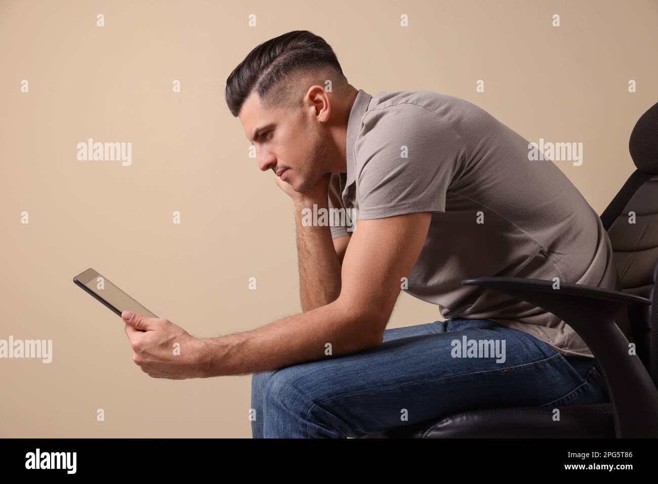 Man with poor posture using tablet while sitting on chair against beige ...