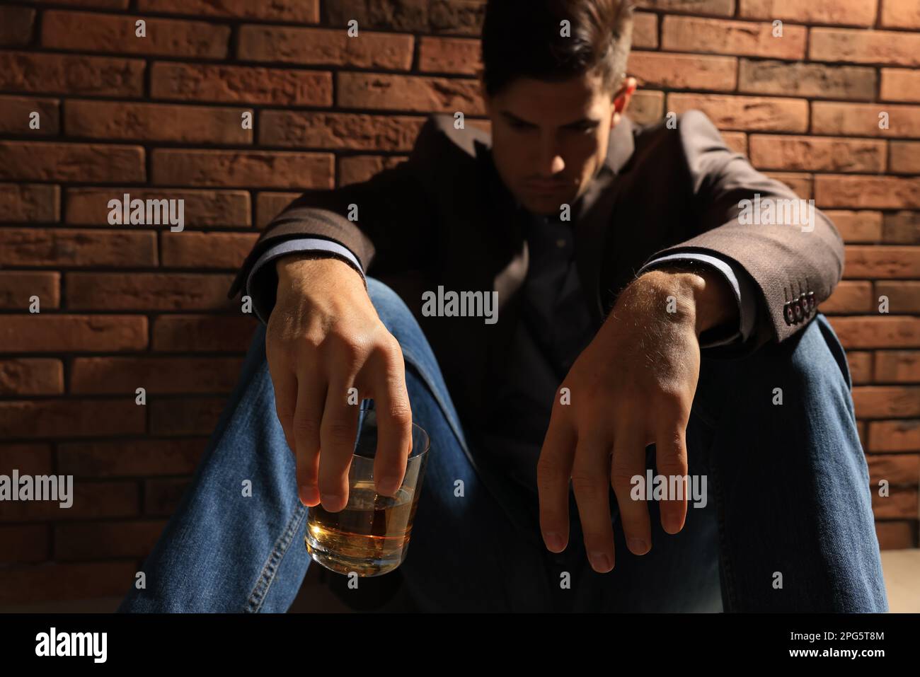 Addicted man near red brick wall, focus on glass of alcoholic drink ...