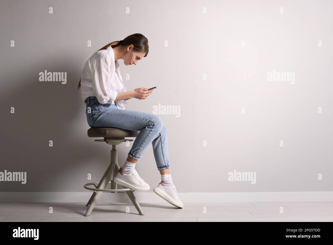 Woman with bad posture using smartphone while sitting on stool near ...