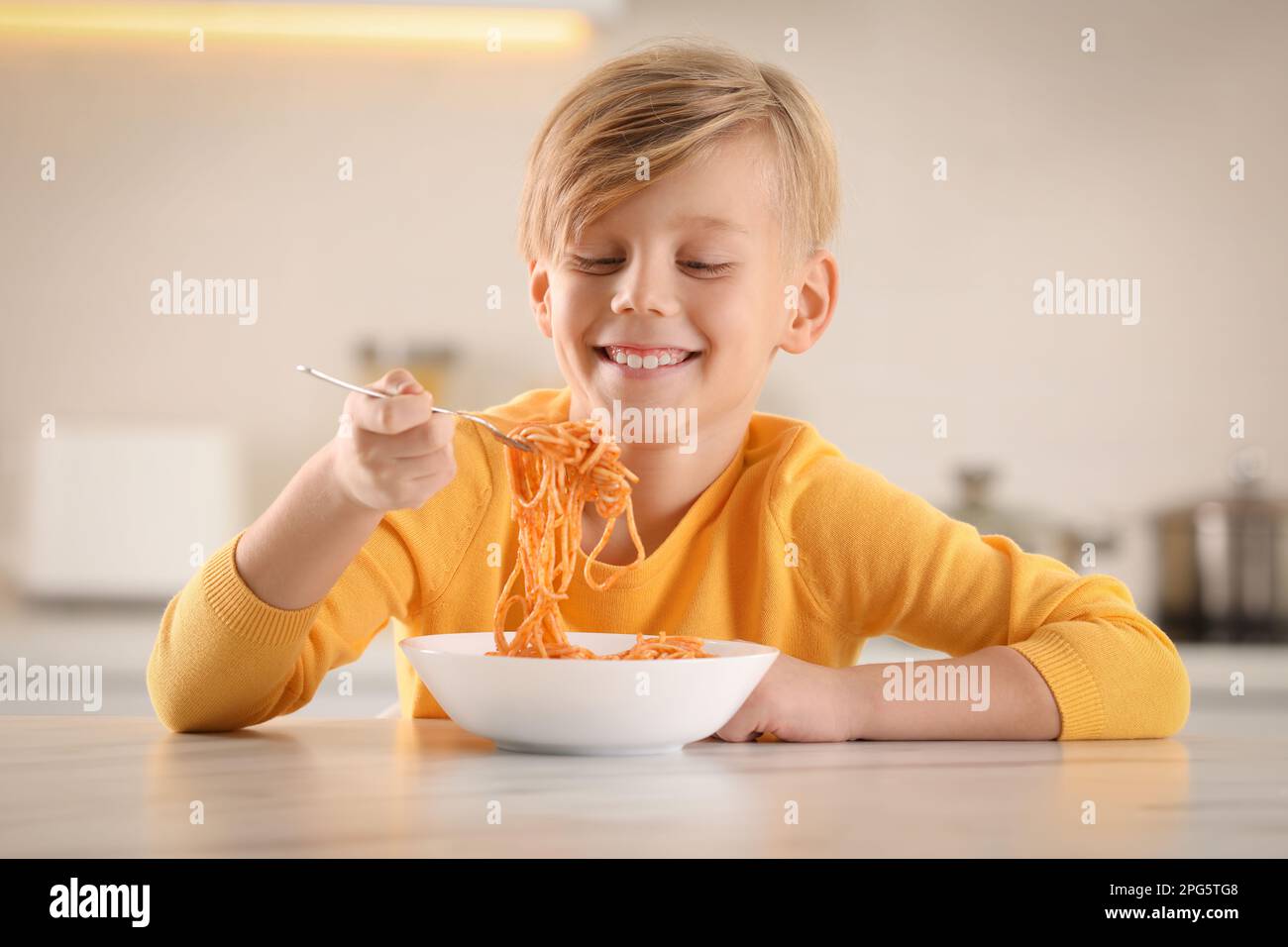 Happy boy eating tasty pasta at table in kitchen Stock Photo - Alamy