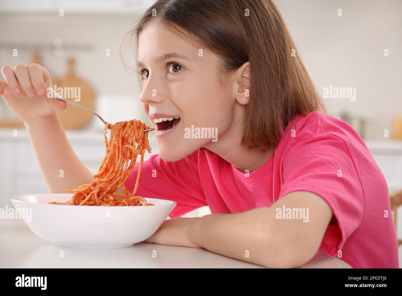 Happy girl eating tasty pasta at table in kitchen Stock Photo - Alamy