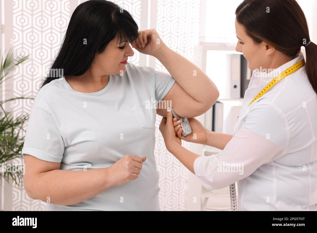Nutritionist measuring overweight woman's body fat layer with caliper ...