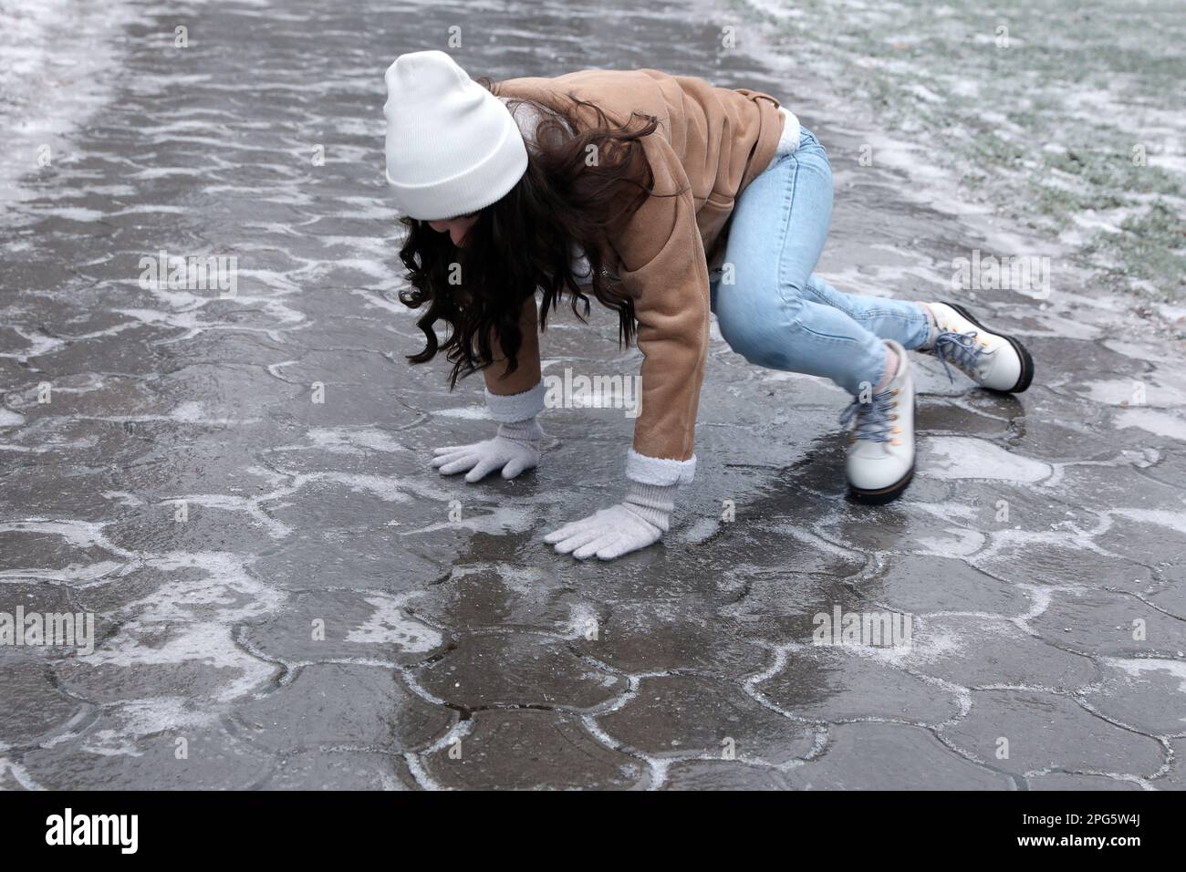 Young woman trying to stand up after falling on slippery icy pavement ...