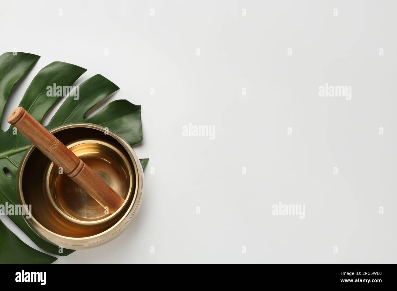 Golden singing bowls, mallet and monstera leaf on white background ...