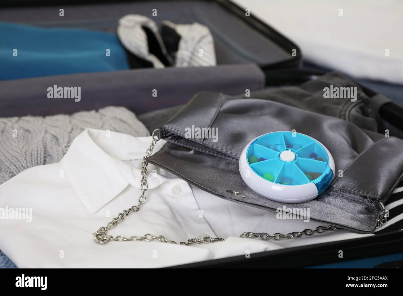 Open suitcase with packed clothes, accessories and pill box, closeup ...
