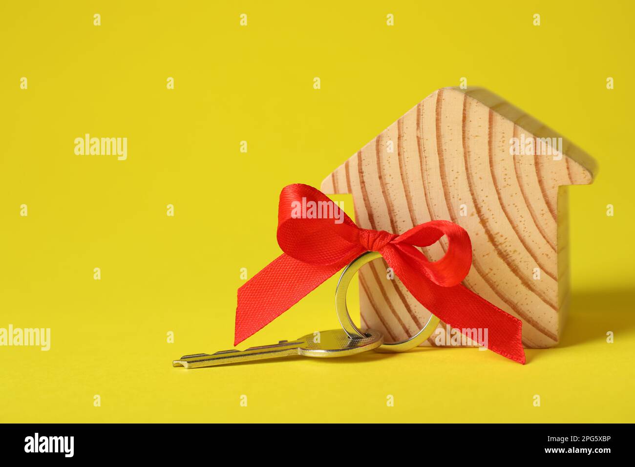 Wooden house model with red bow and key on yellow background, space for ...