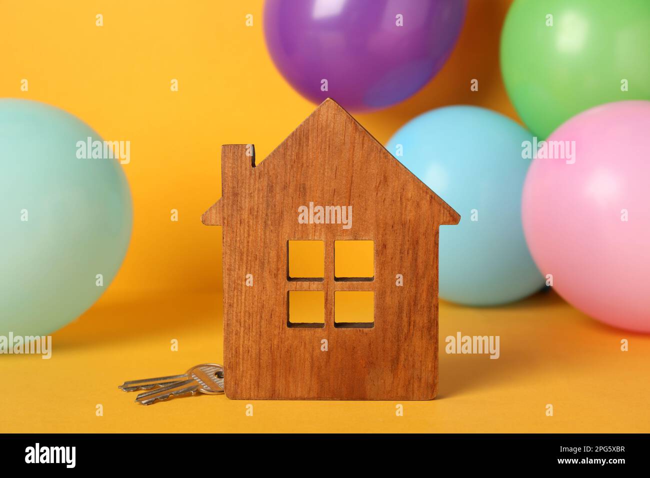 House model with keys and blurred balloons on yellow background ...
