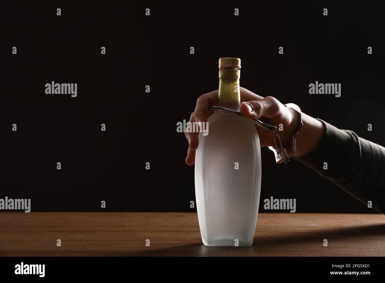 Alcohol addiction. Man handcuffed to bottle of vodka at wooden table ...