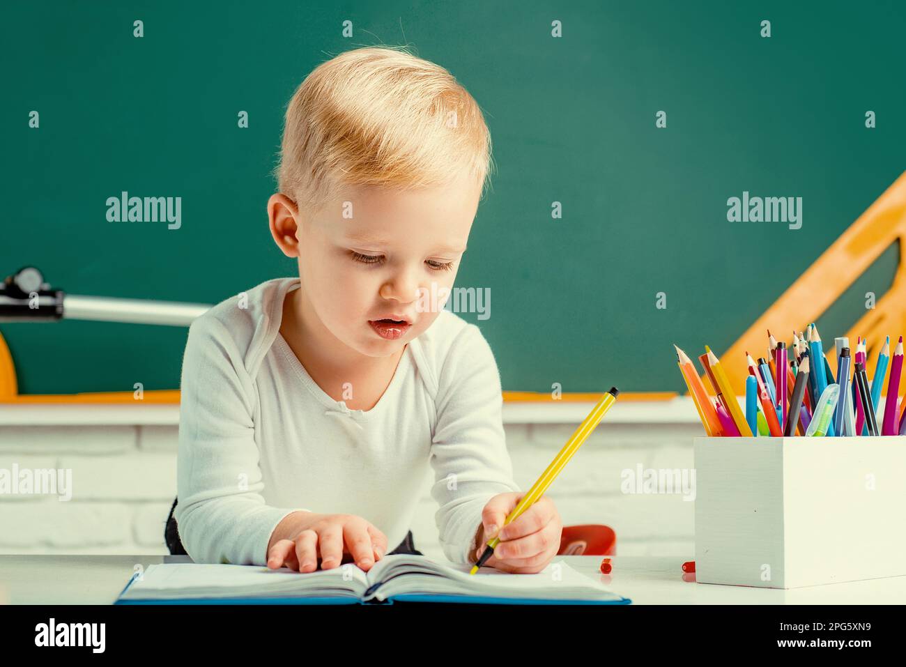 Cute child boy in classroom near blackboard desk. Chalkboard copy space ...