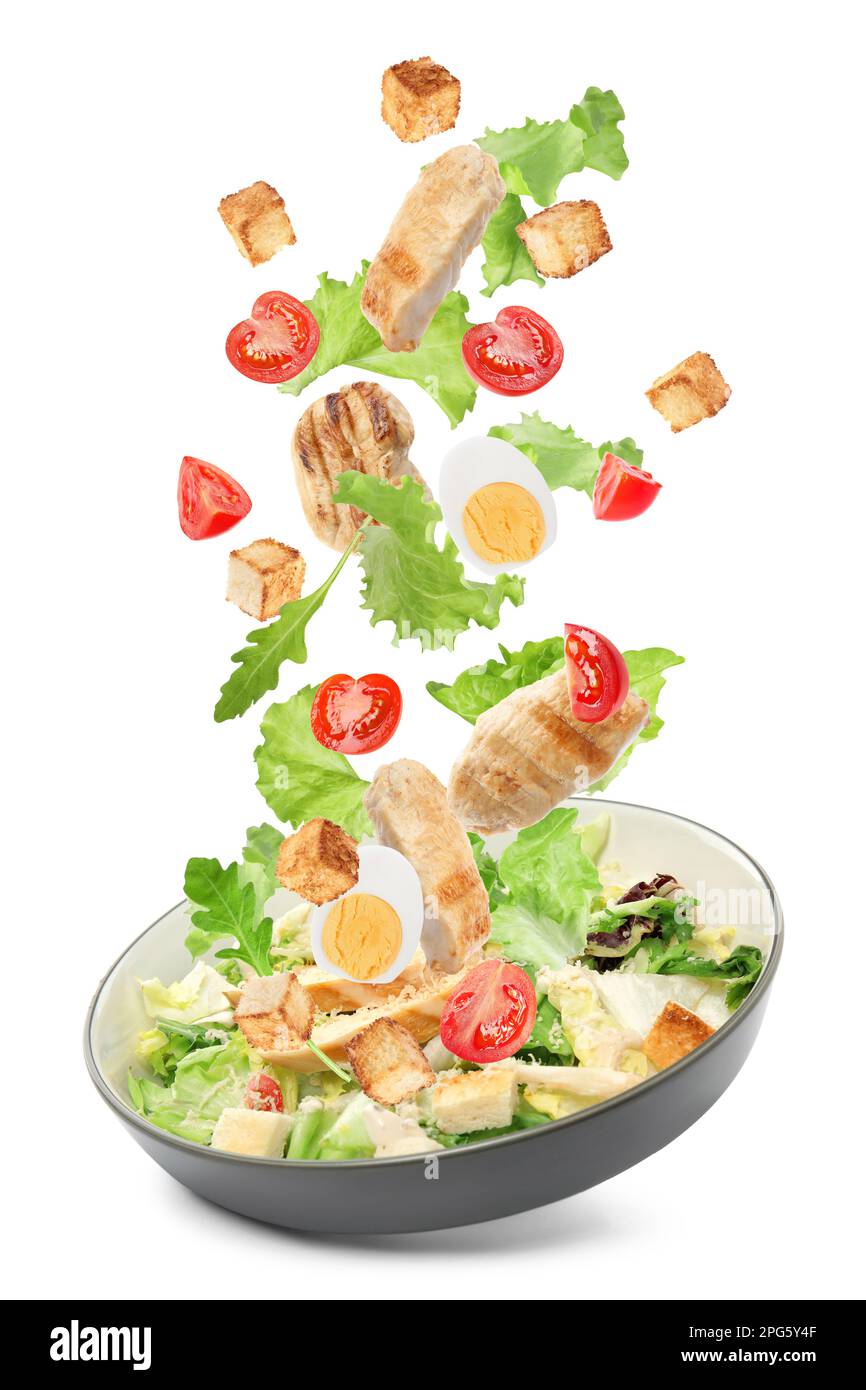 Tasty ingredients for Caesar salad falling into plate on white ...