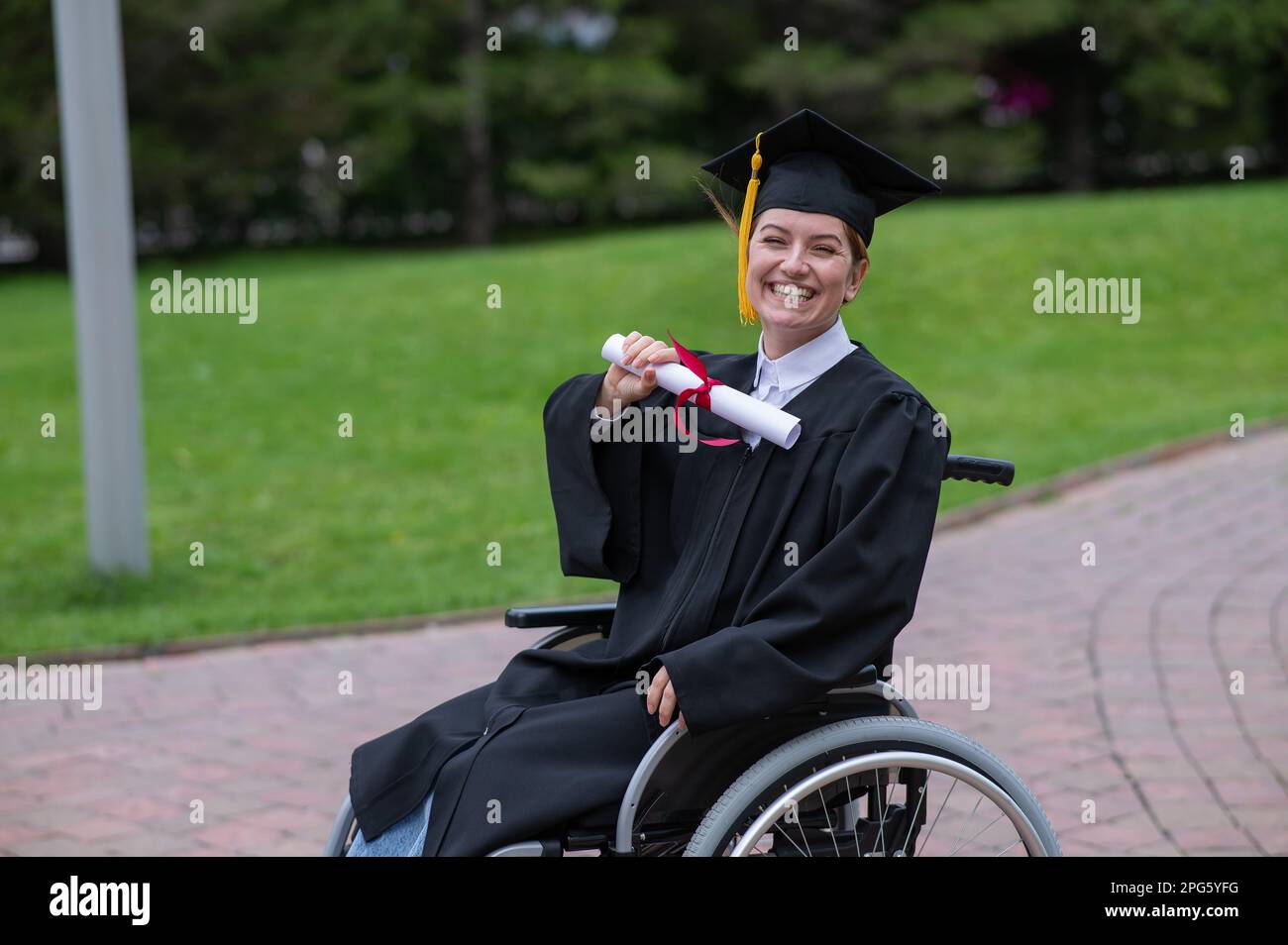 Caucasian woman in a wheelchair in a graduate costume rejoices at ...