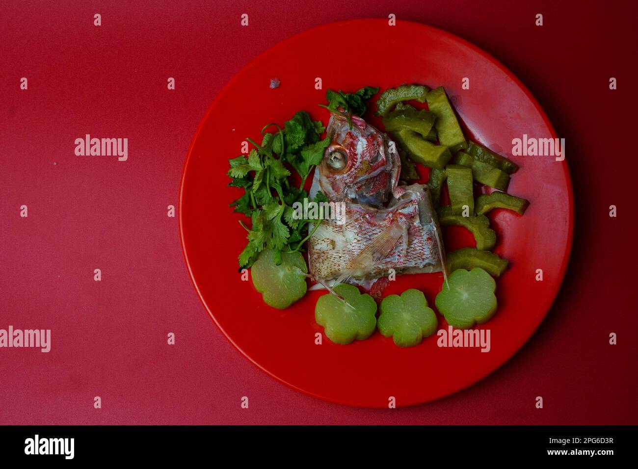 Steamed red snapper head with bitter gourds and chayote on red plate ...