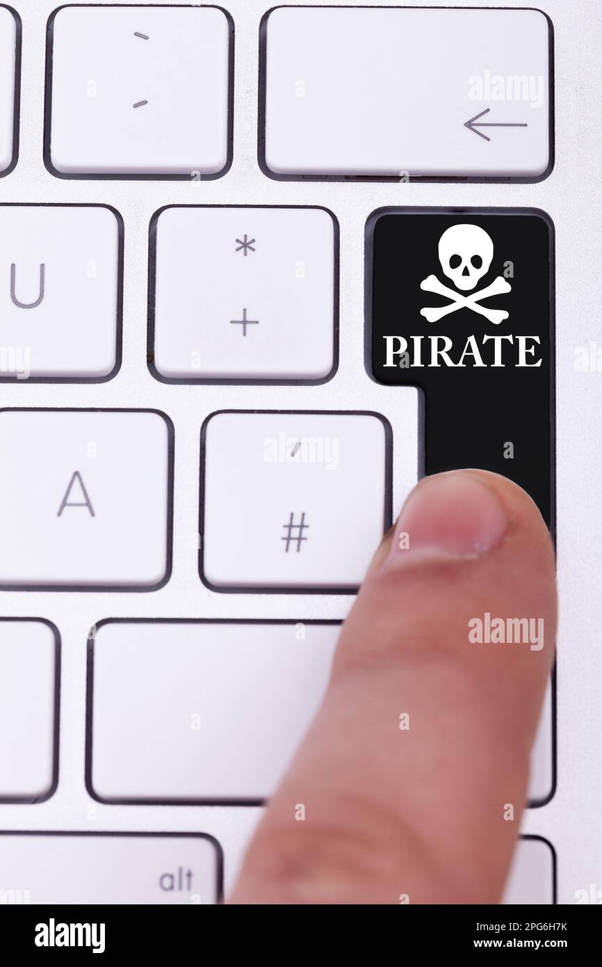 Finger pressing the pirate button and skull on keyboard. Illegall data ...