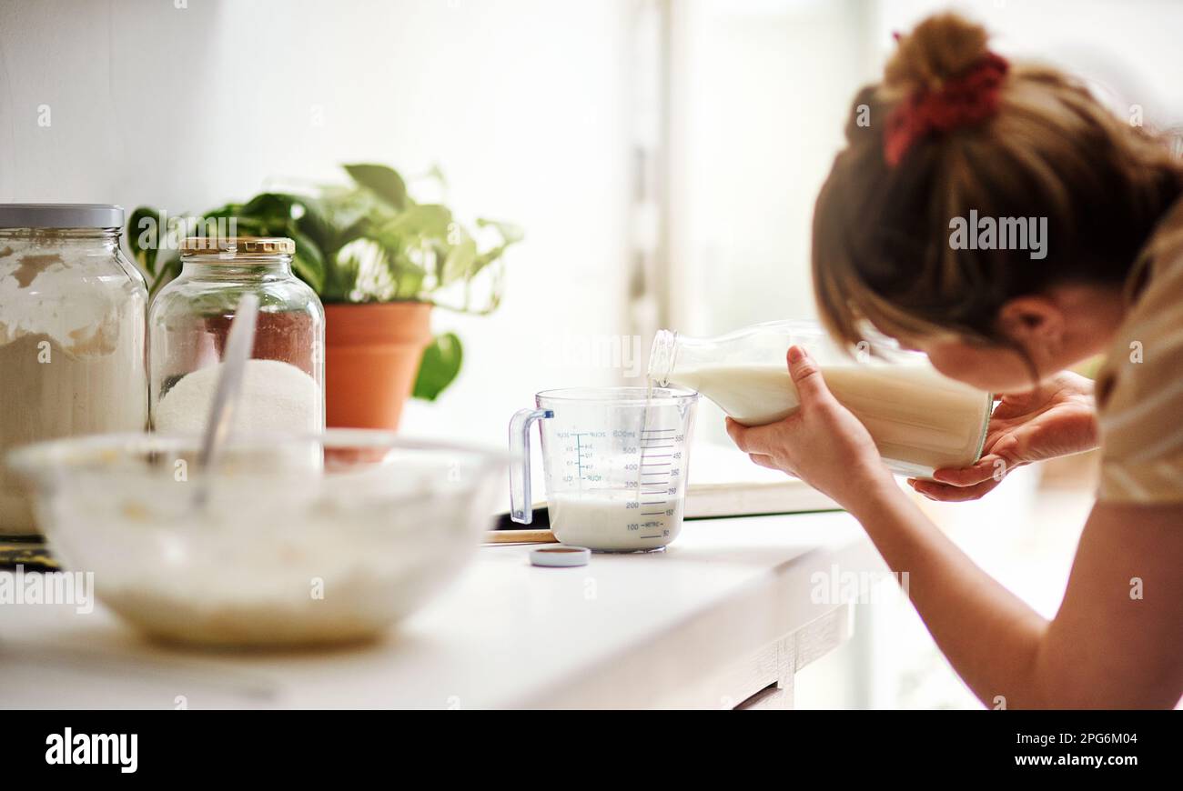 Baking is a science. a young woman measuring milk while baking at home ...
