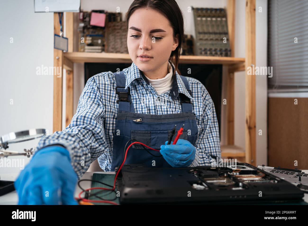Female worker testing laptop motherboard using multimeter while working ...
