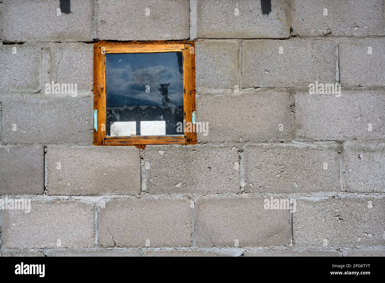 A rough cinder block wall with a small window reflecting the sky of ...