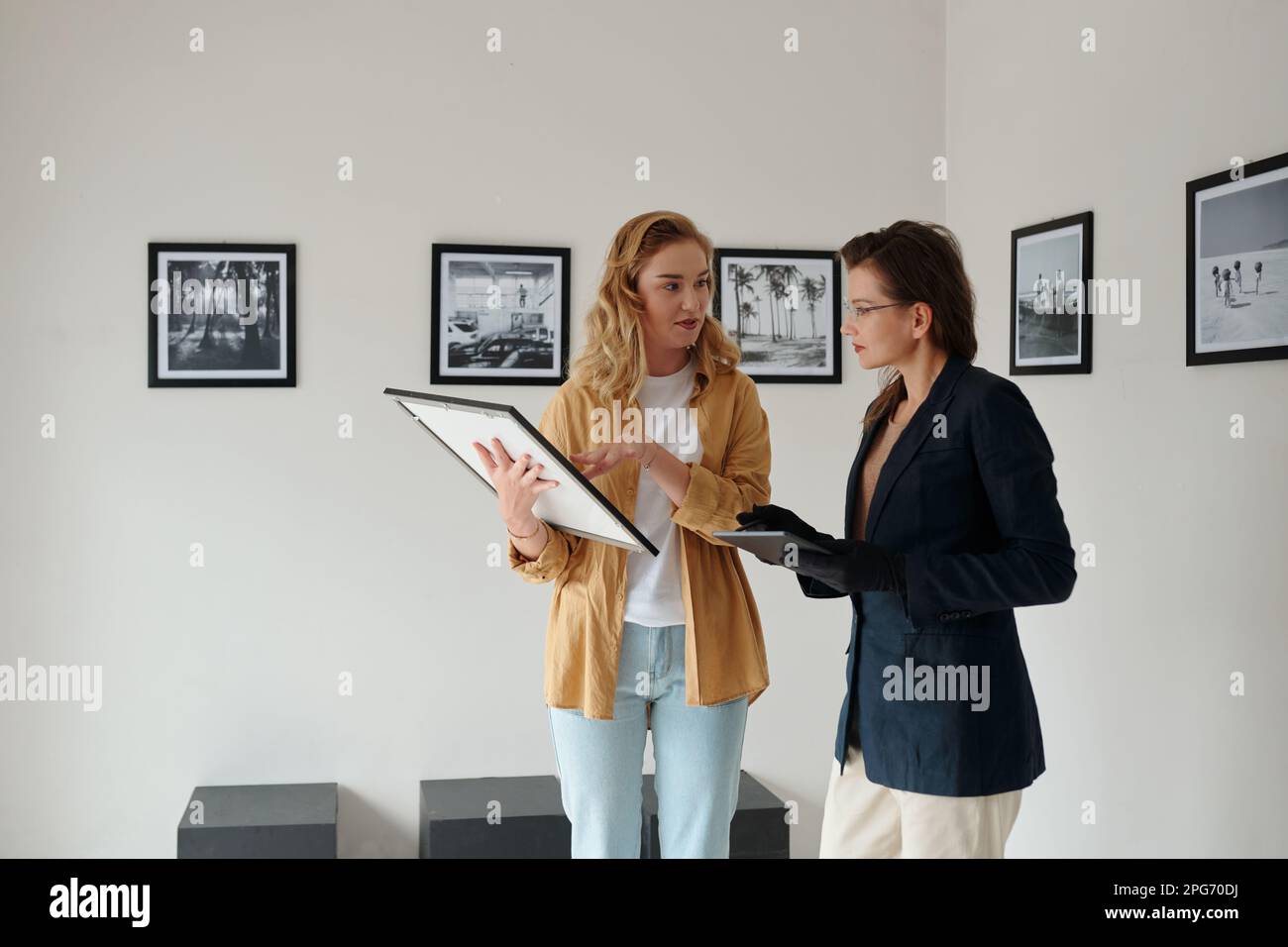 Two female workers of art gallery discussing restored picture and ...