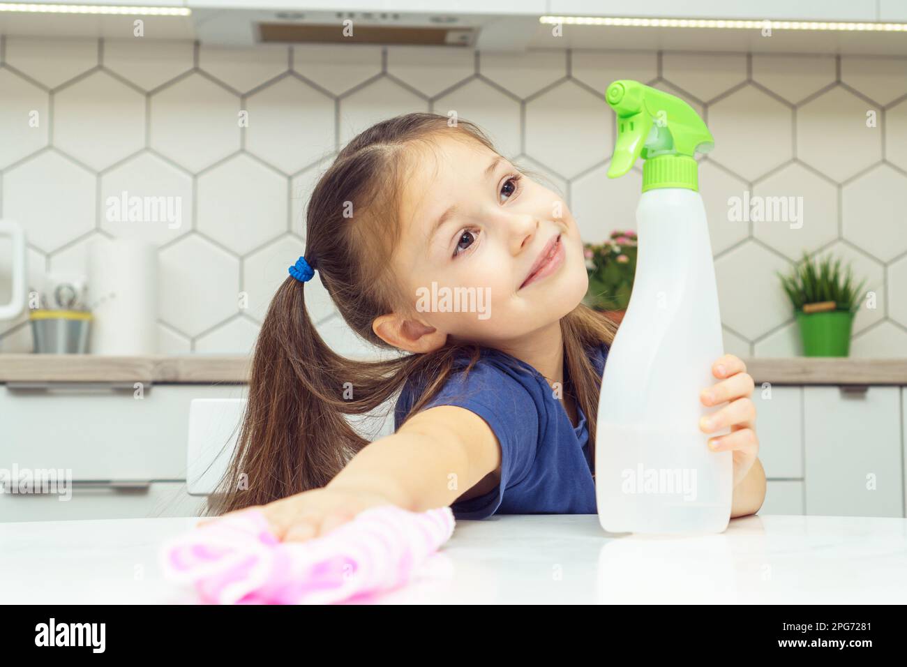 Nice little girl with detergent sprayer and household rag wipe table ...