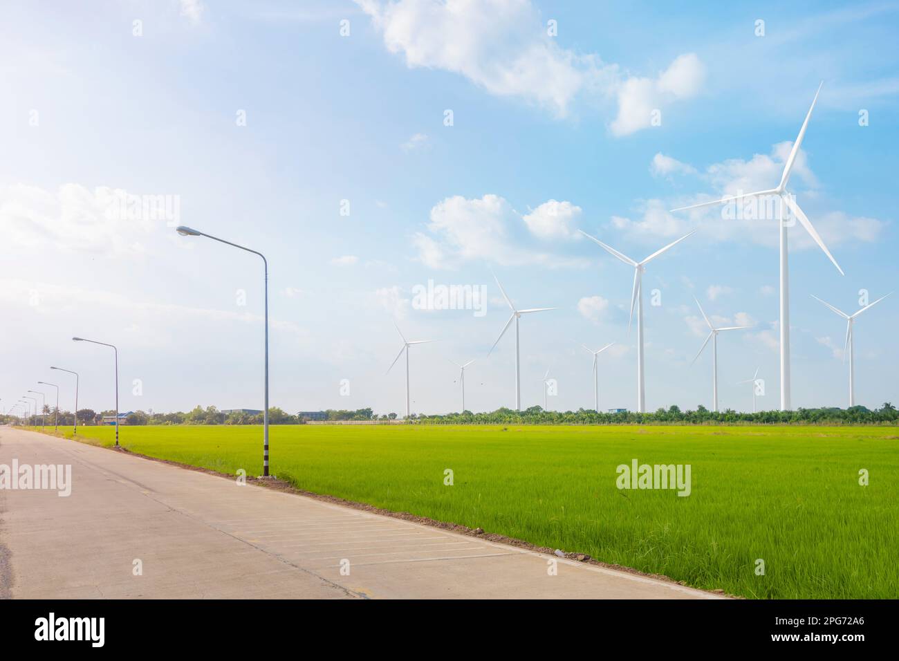 Concrete road in rural Thailand through green fields and wind turbine ...