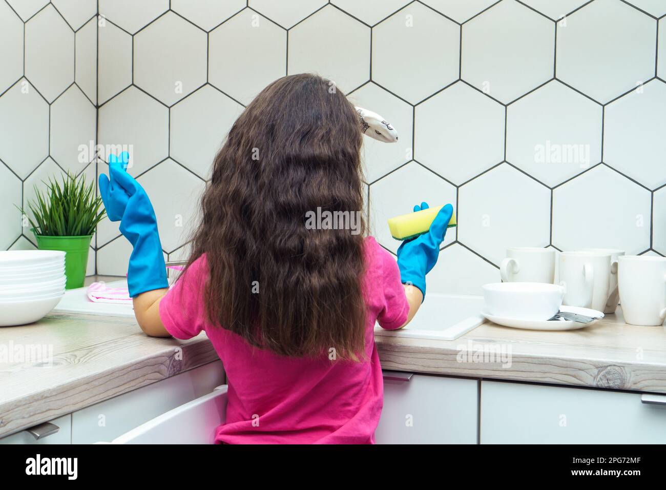Little girl in household gloves washing up tableware with dishwashing ...