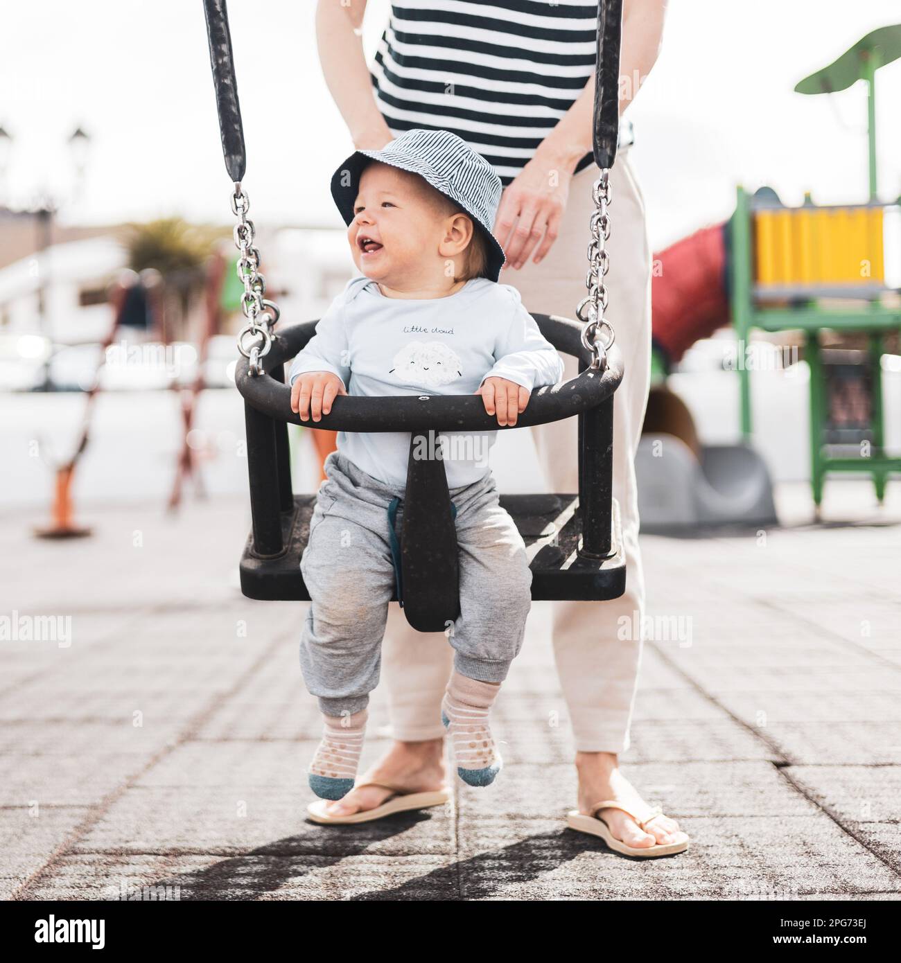 Mother pushing her infant baby boy child on a swing on playground ...