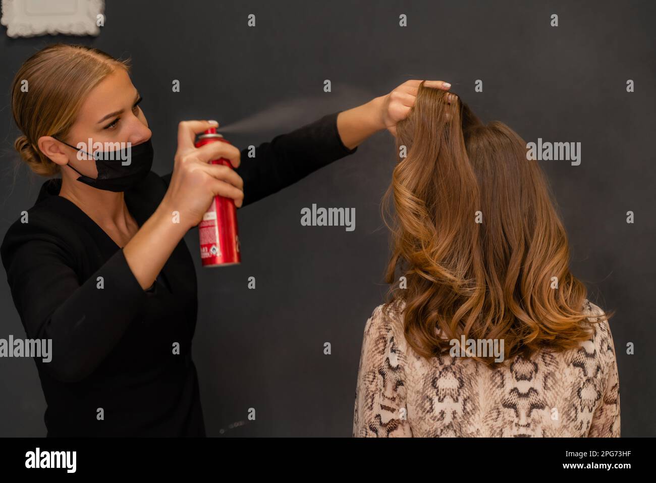 Women salon hairstyle. Hairdresser uses hairspray on client's hair in ...