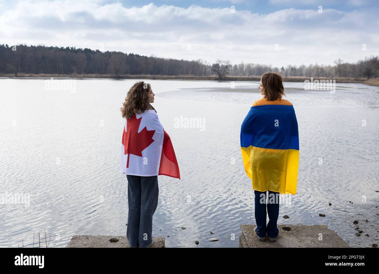 Two women with Ukrainian and Canadian flags behind backs stand together ...