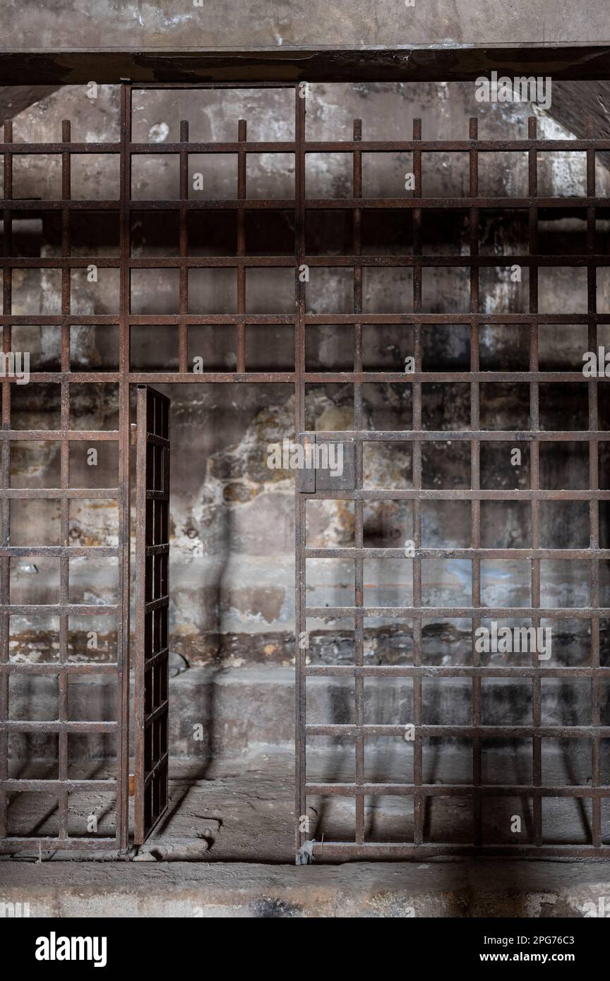 An aged prison cell block featuring a barred entrance with an open door ...
