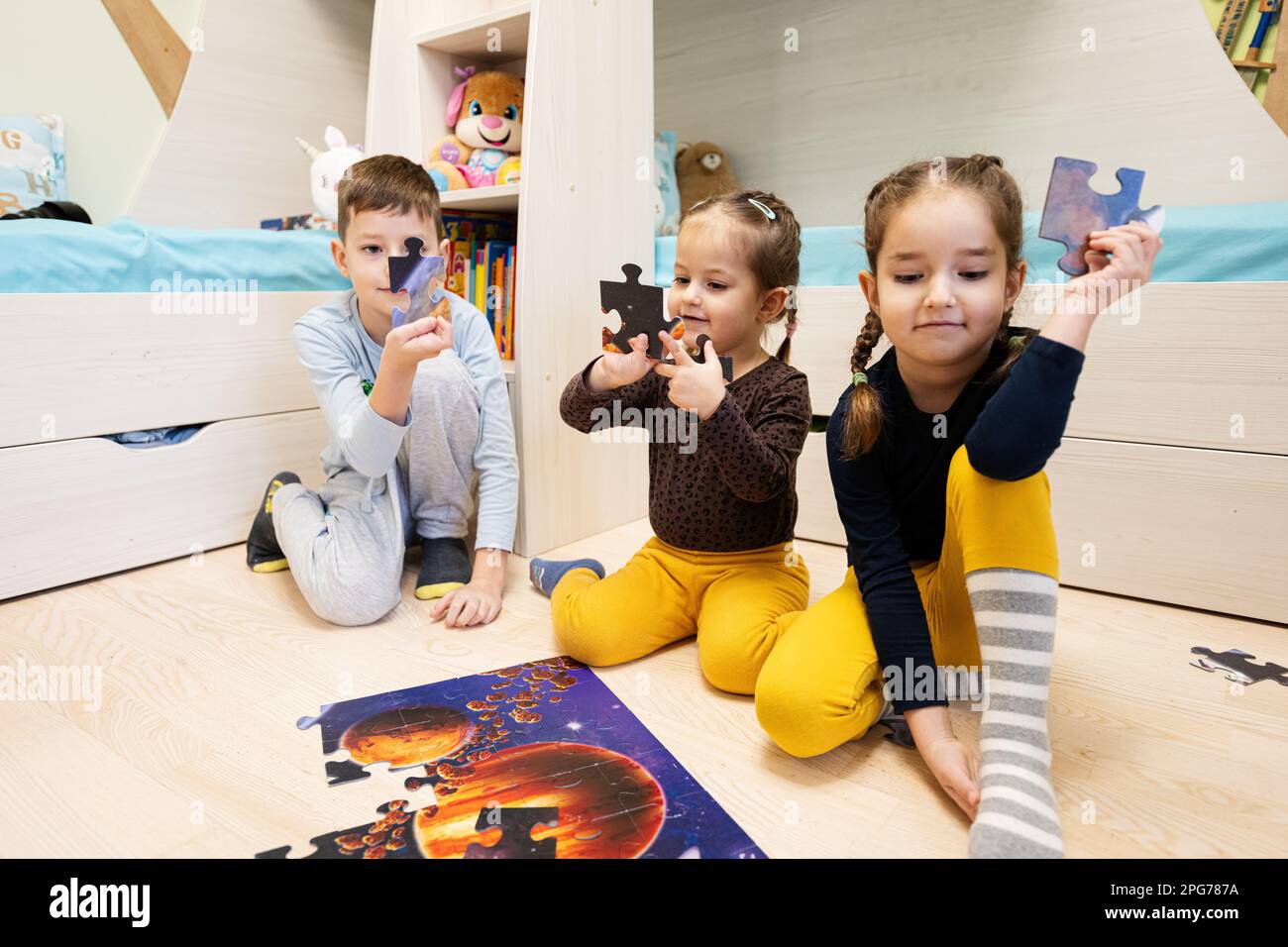 Children connecting jigsaw puzzle pieces in a kids room on floor at ...