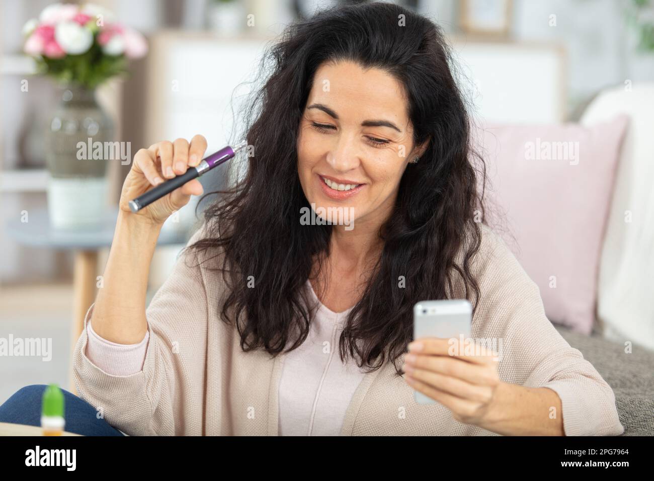 mature brunette looking onto her smartphone screen while vaping Stock ...