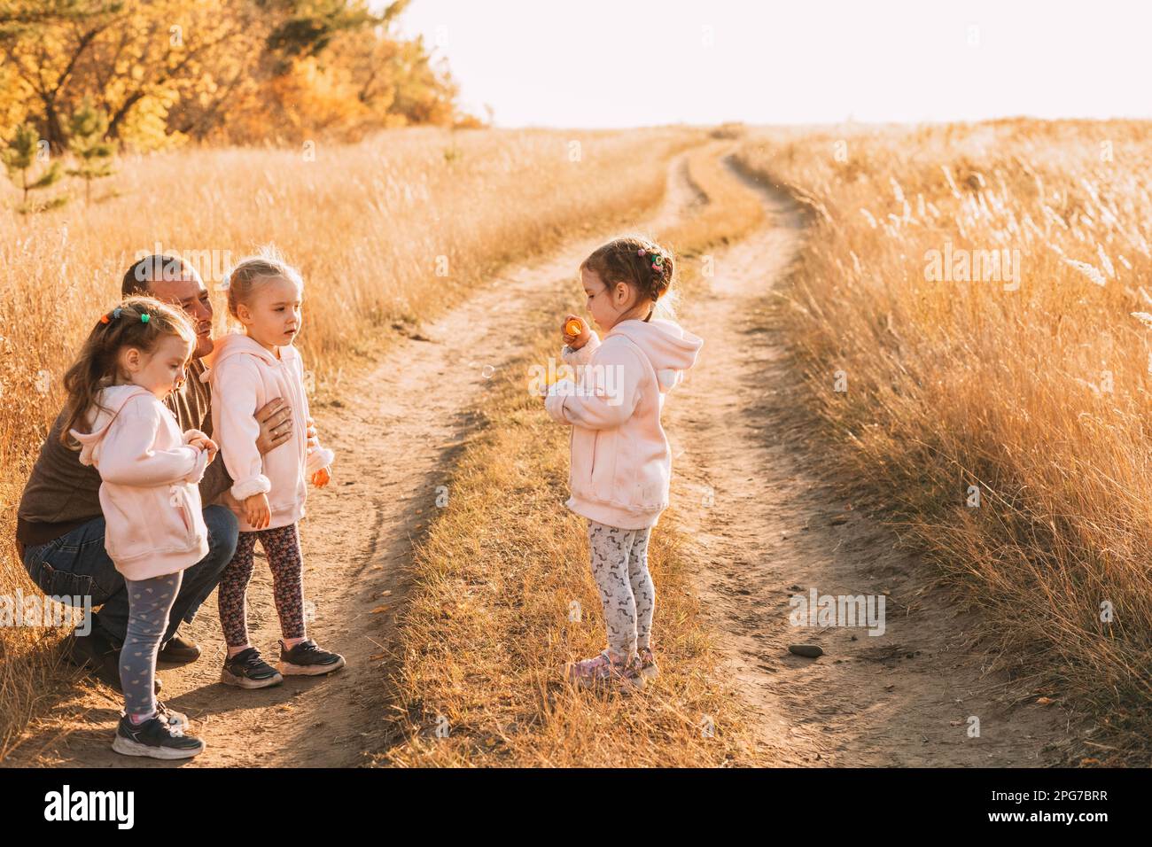 Triplets sisters in the field with dad with soap bubbles Stock Photo ...