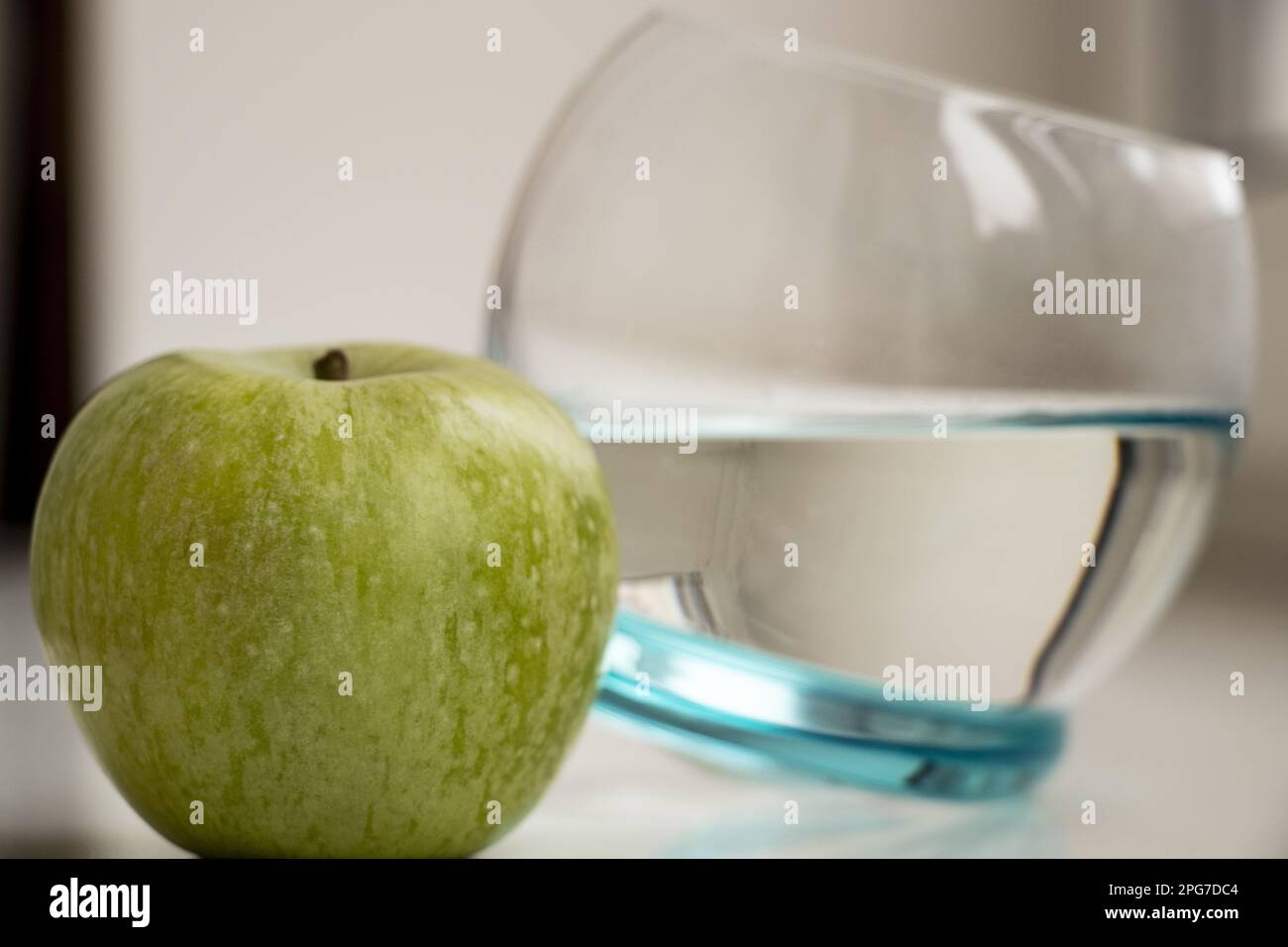 One green apple and a glass of water next to it on a light background ...