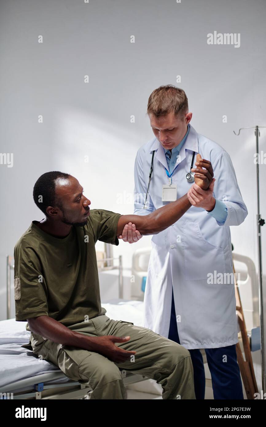Vertical image of doctor in white coat examining the arm of soldier ...