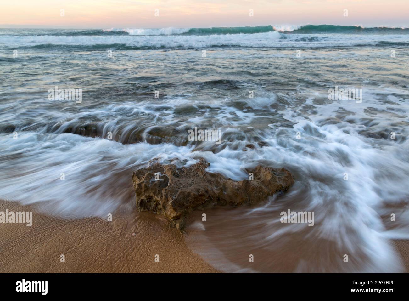 Scenic view of a wave washing over a rock lying on the beach with waves ...