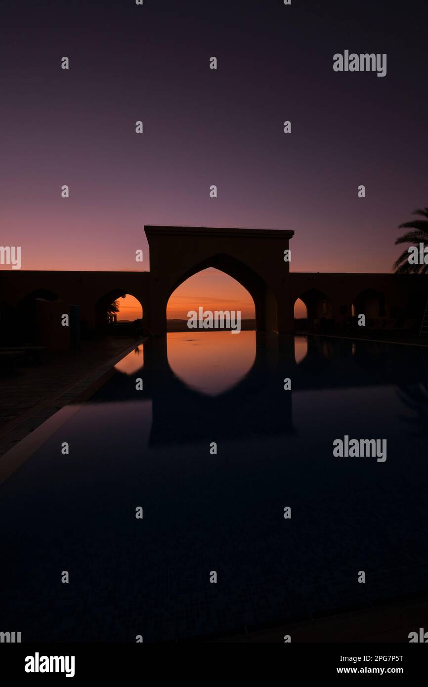Sunrise beyond an archway at the end of an infinity swimming pool. At ...