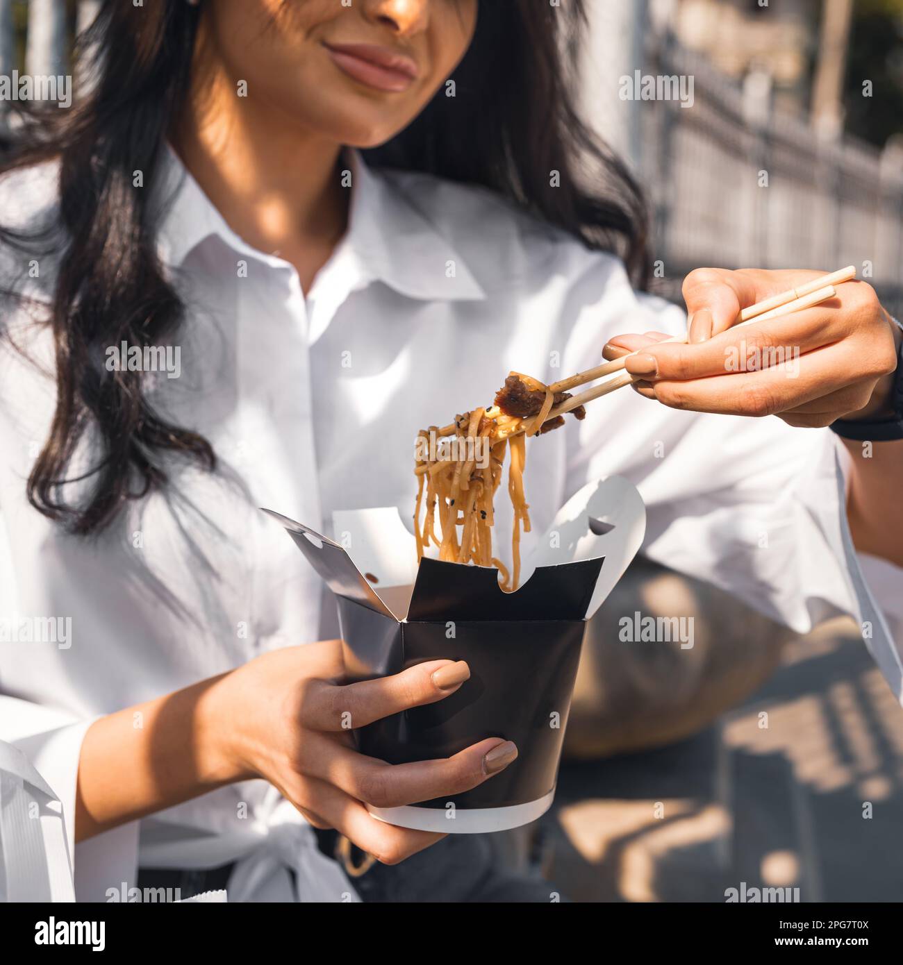 Pretty young woman eating Asian food with Wok noodles using chopsticks ...