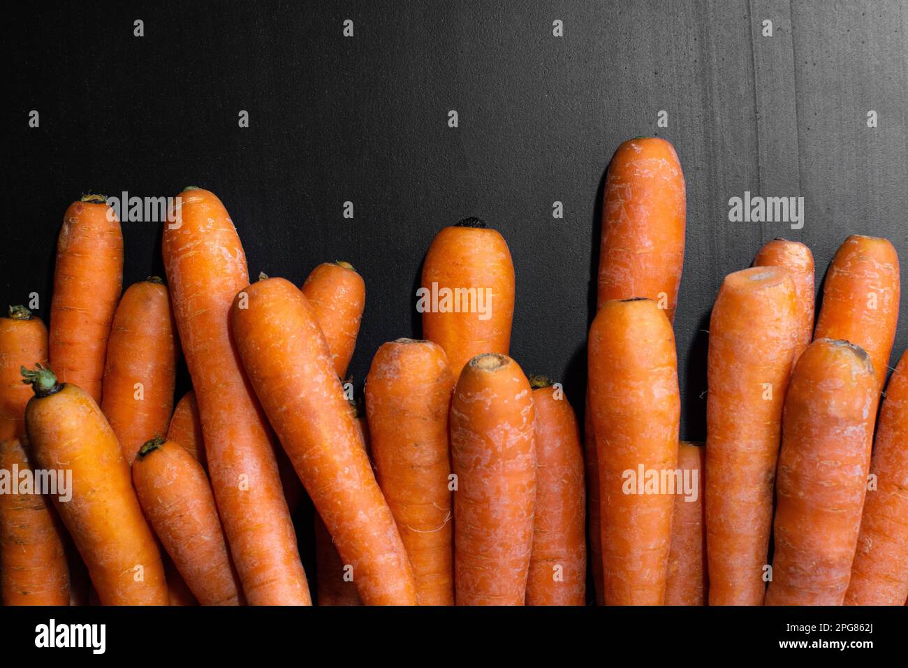 An abundance of fresh carrots arranged in a neat stack, on a black ...