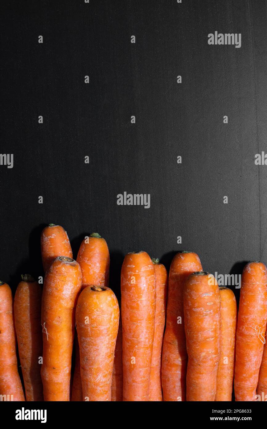 An abundance of fresh carrots arranged in a neat stack, on a black ...