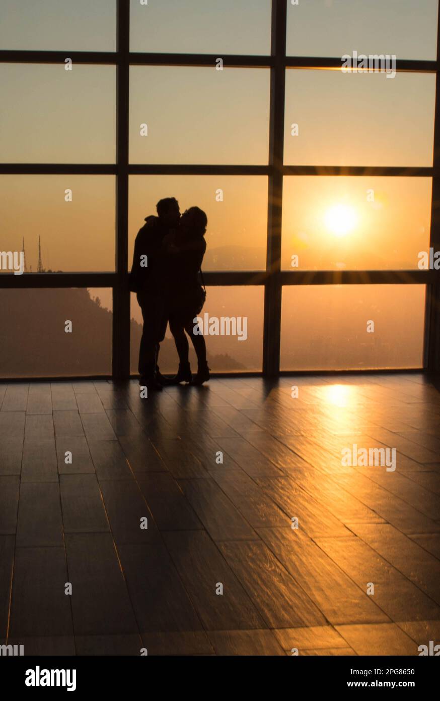 A vertical shot of a couple embracing while looking out a window at the ...