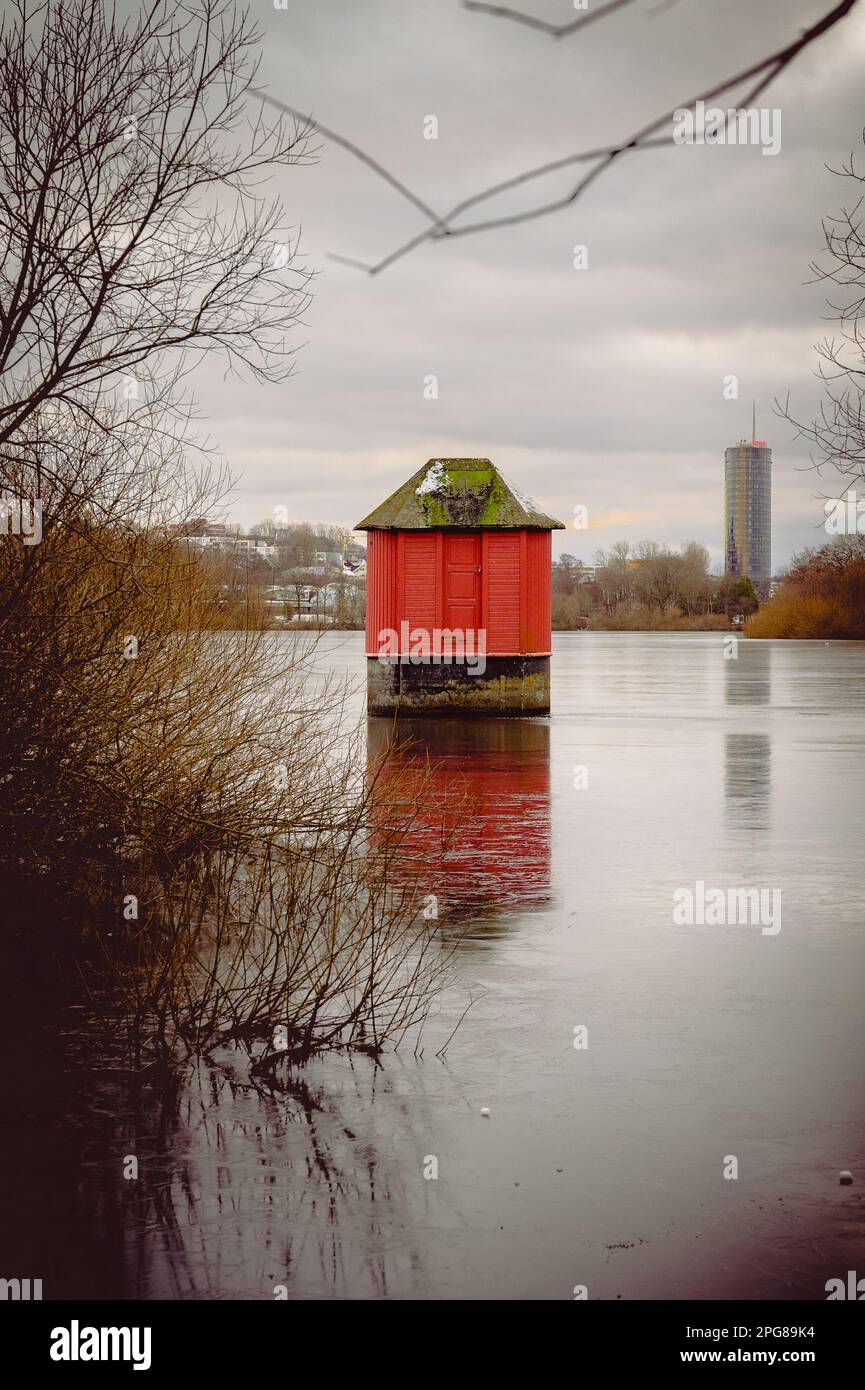 A vivid red wooden hut stands in the shallow waters of a tranquil river ...