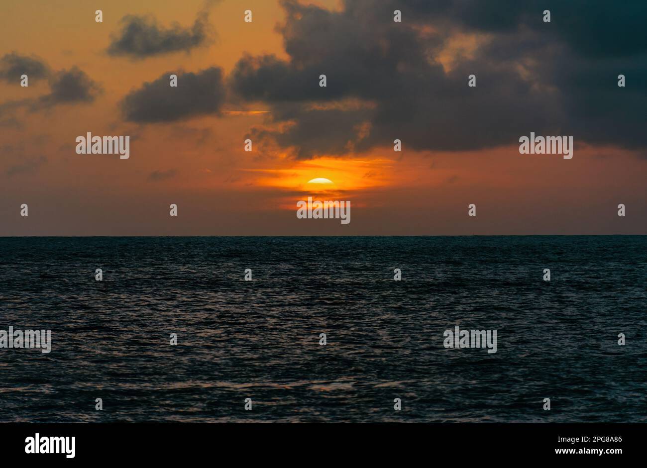 Amazing sky with sun behind clouds above horizon over ocean at dusk ...