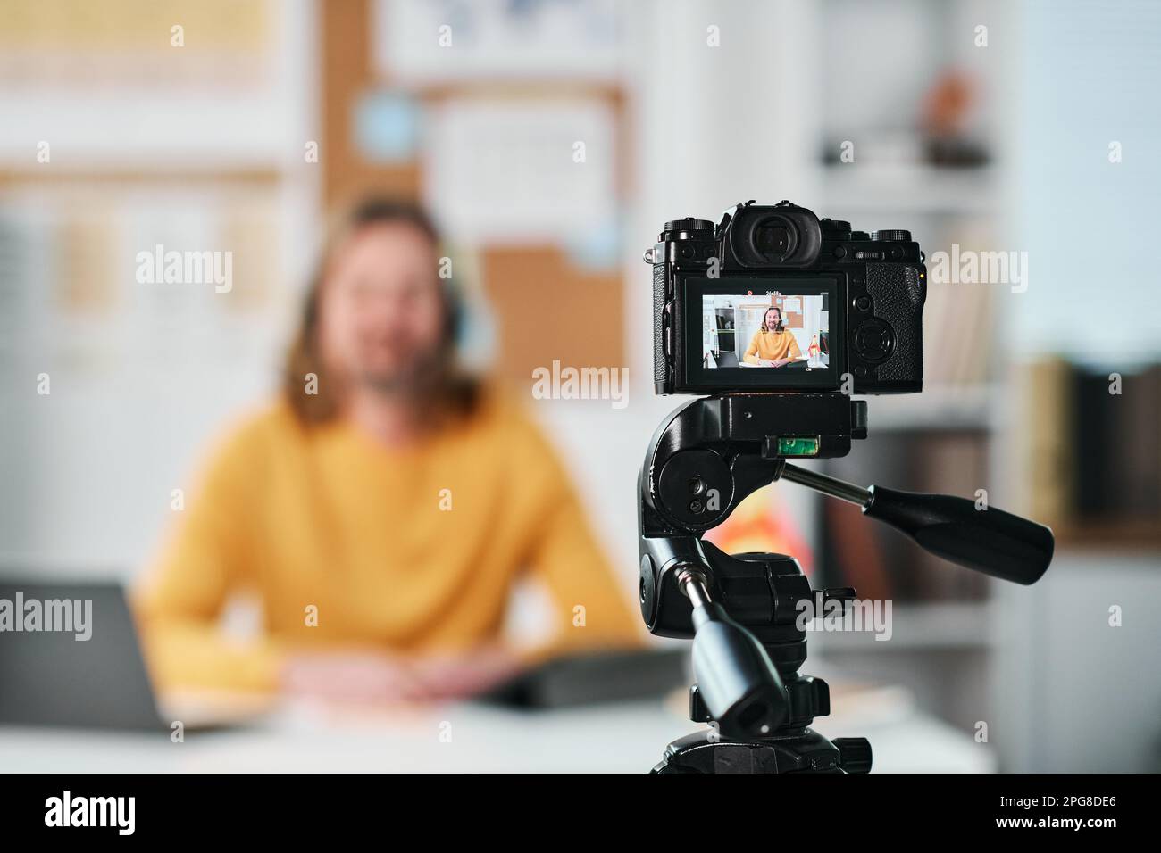 Mature man sitting at table in the classroom and recording lesson for ...