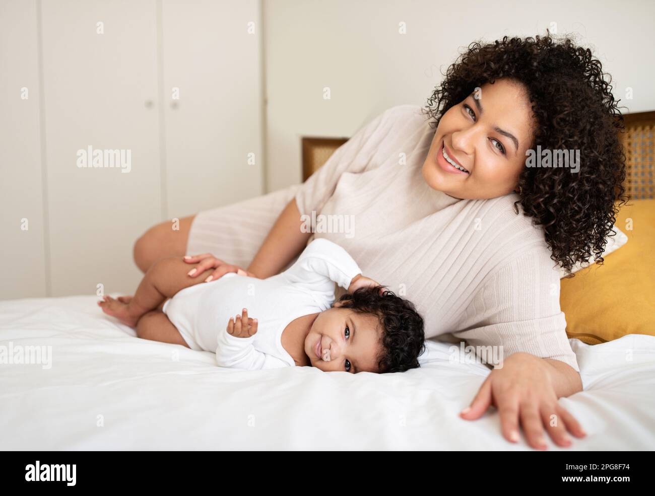 Smiling loving young african american female lies on bed with baby ... Smiling loving young african american female lies on bed with baby ...